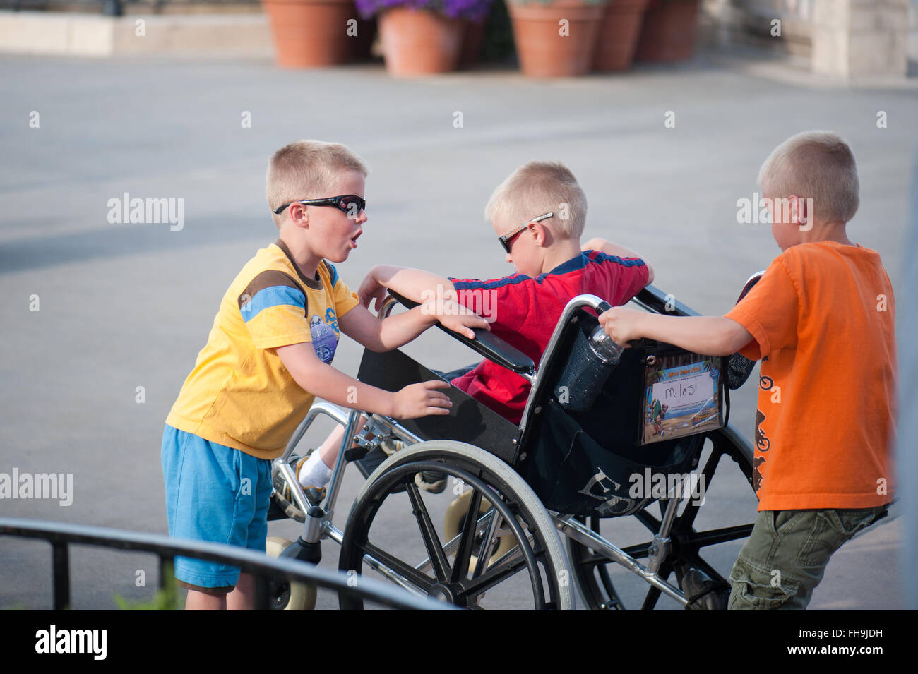 Three young kids having fun playing together with a handicap wheelchair ...