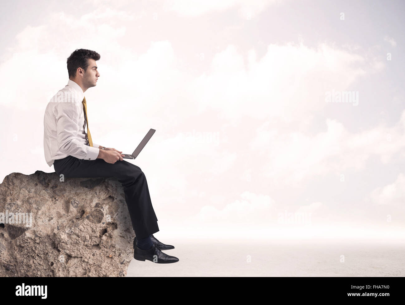 Business man sitting on stone edge Stock Photo - Alamy