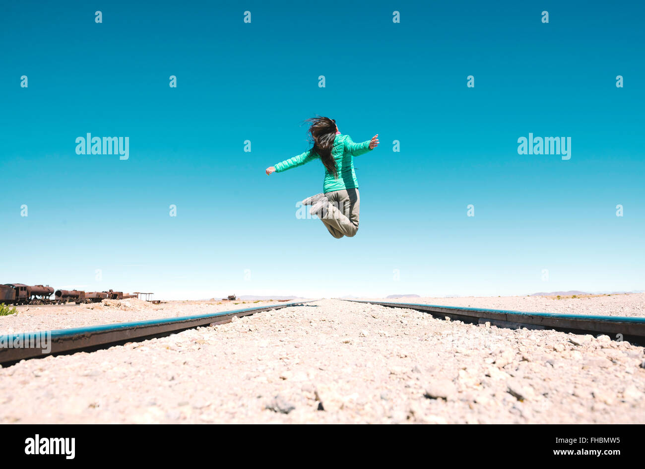 Bolivia, Uyuni train cemetery, woman jumping over the train tracks ...
