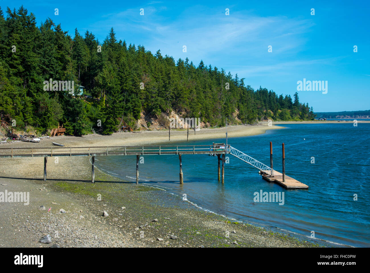 boat dock at low tide on rocky beach near lush green forest under blue ...