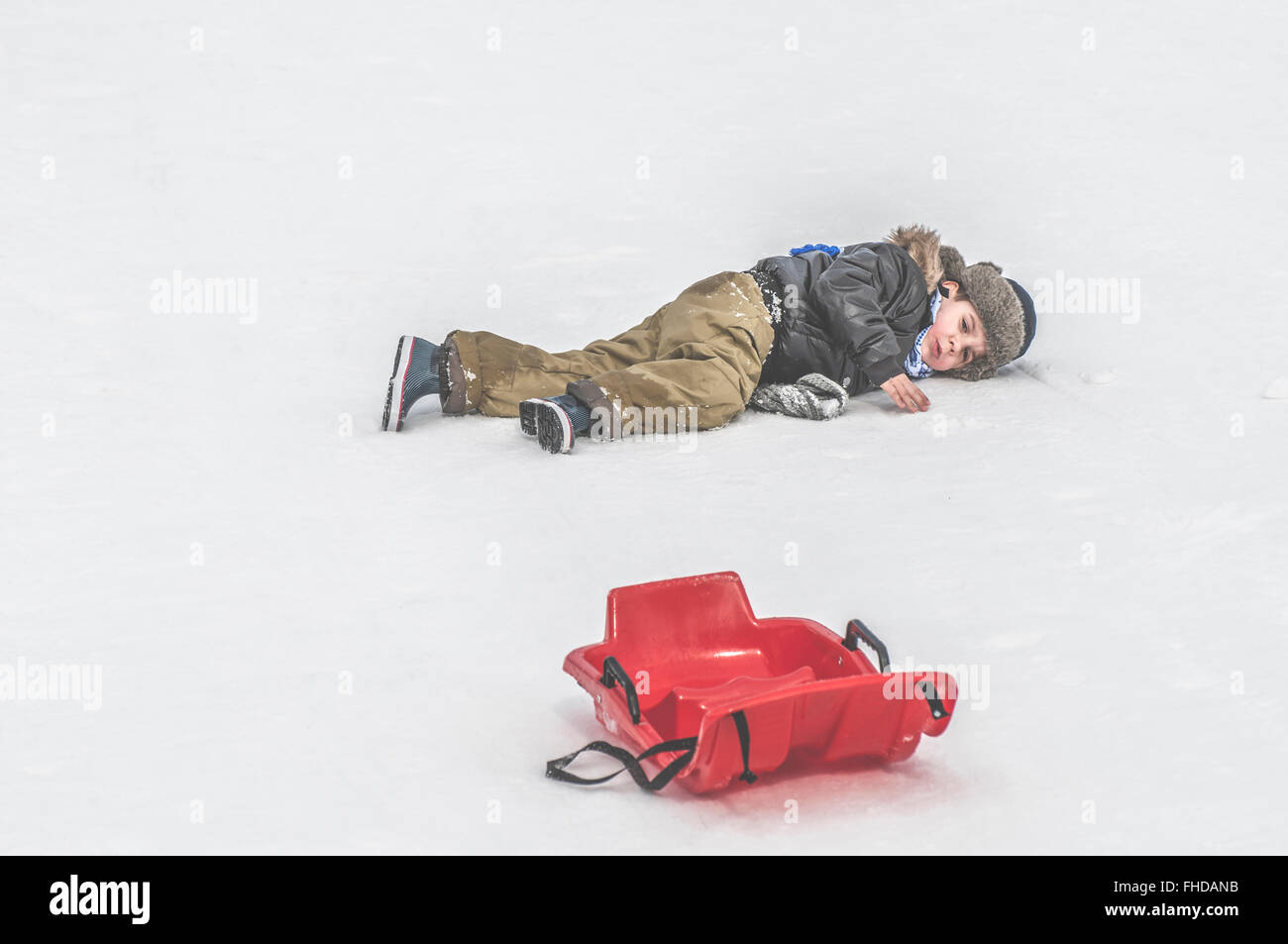 Boy lying in snow next to sledge Stock Photo - Alamy