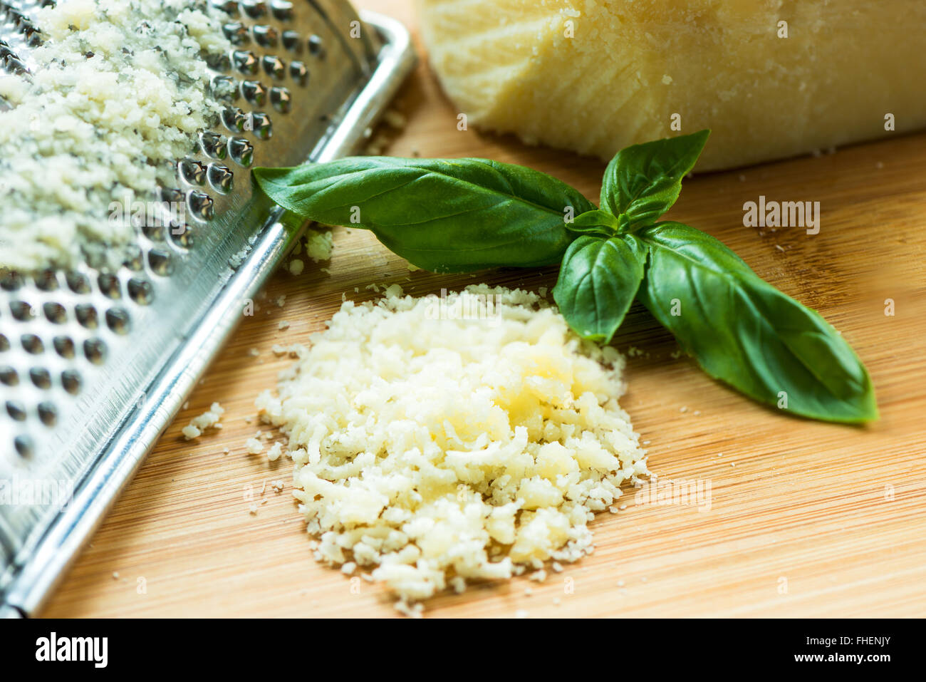 Heap of grated Parmesan on wooden background with leaf of basil and ...