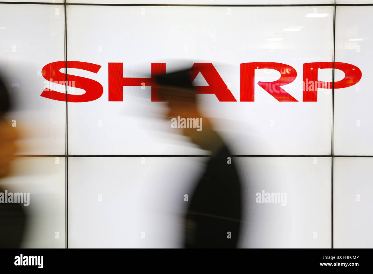 A man walks past display showing a logo of Sharp Corp in Tokyo, Japan ...