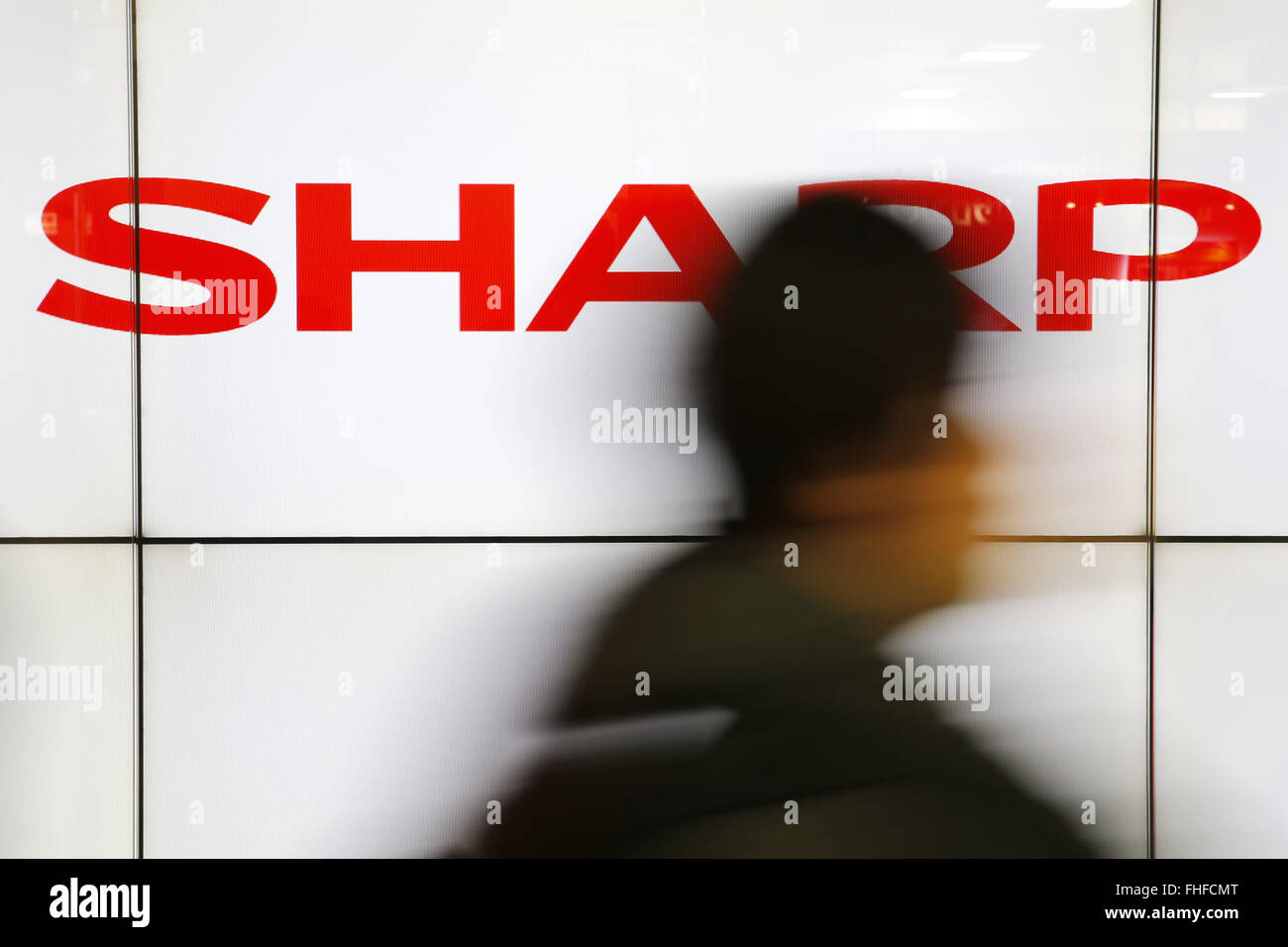 A man walks past display showing a logo of Sharp Corp in Tokyo, Japan ...