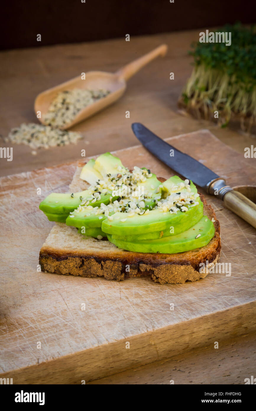 Half slice of toasted bread with acocado and hemp seeds on wooden board ...