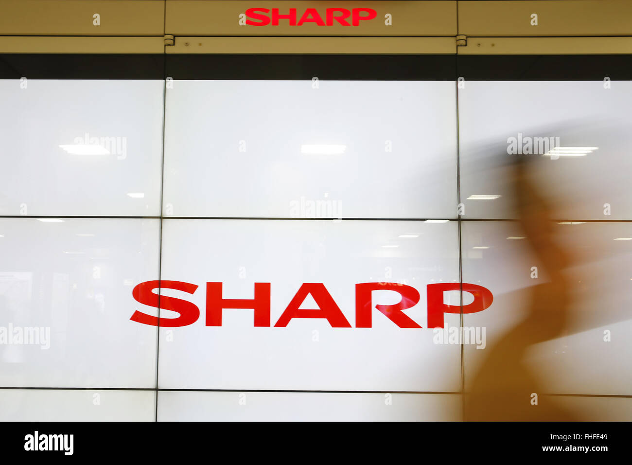 A man walks past display showing a logo of Sharp Corp in Tokyo, Japan ...