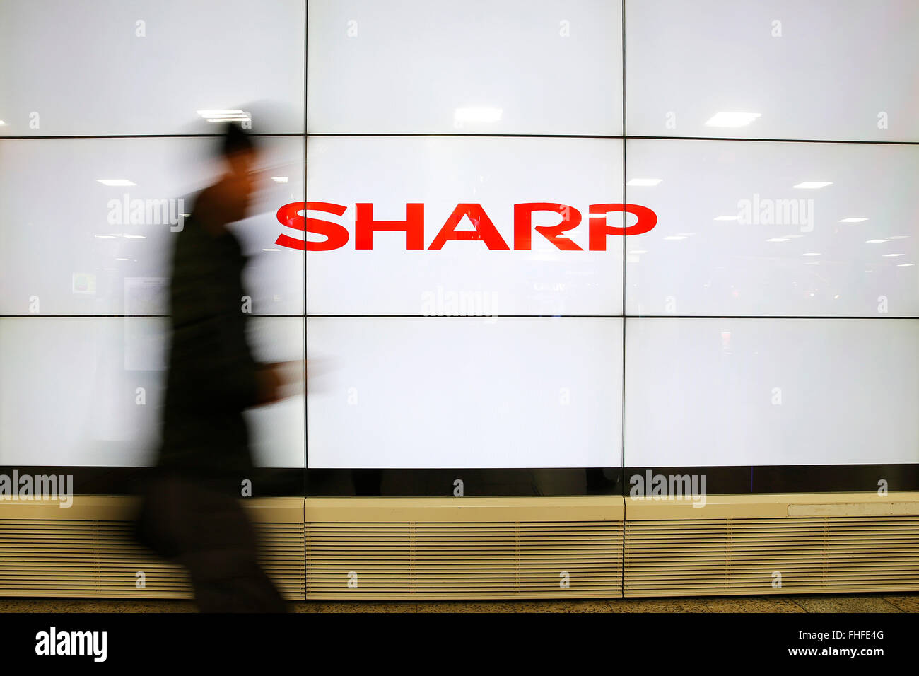 A man walks past display showing a logo of Sharp Corp in Tokyo, Japan ...