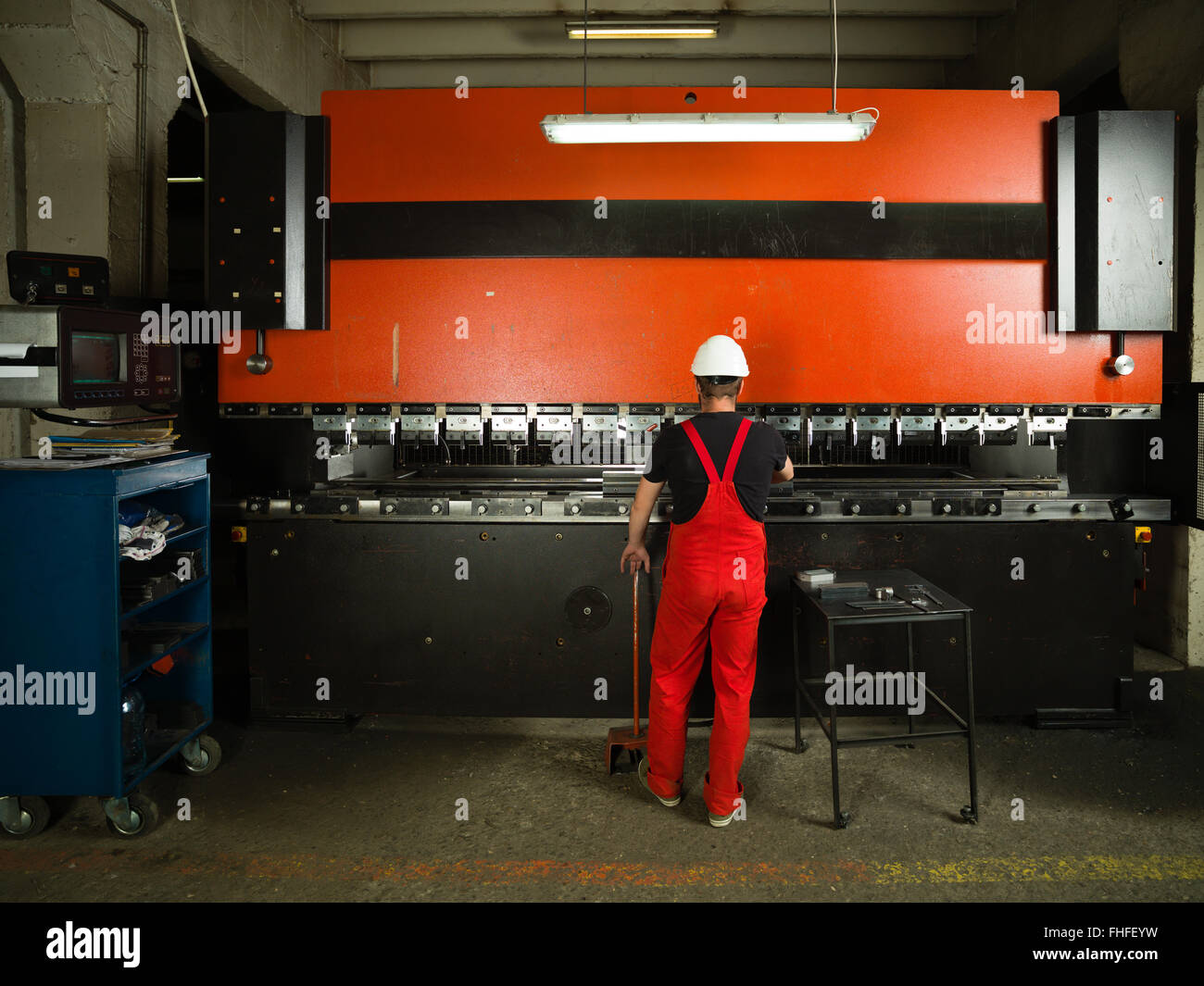 back side view of a worker, standing, wearing red overalls, and a white ...