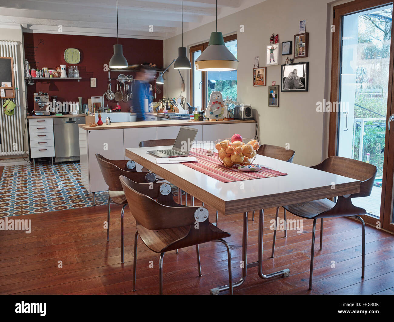 Laptop on dining table in open plan kitchen with man in background ...