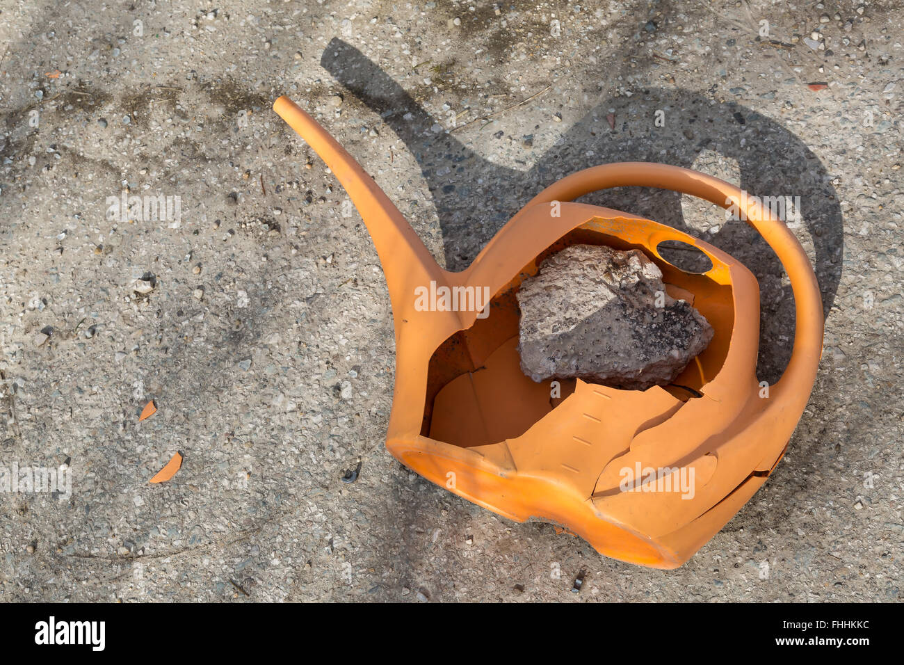 Broken orange watering can and rock Stock Photo - Alamy