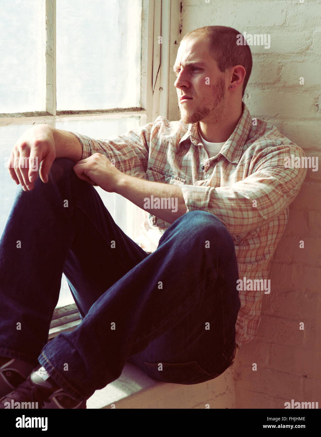 A pensive looking man sitting on a window ledge Stock Photo - Alamy