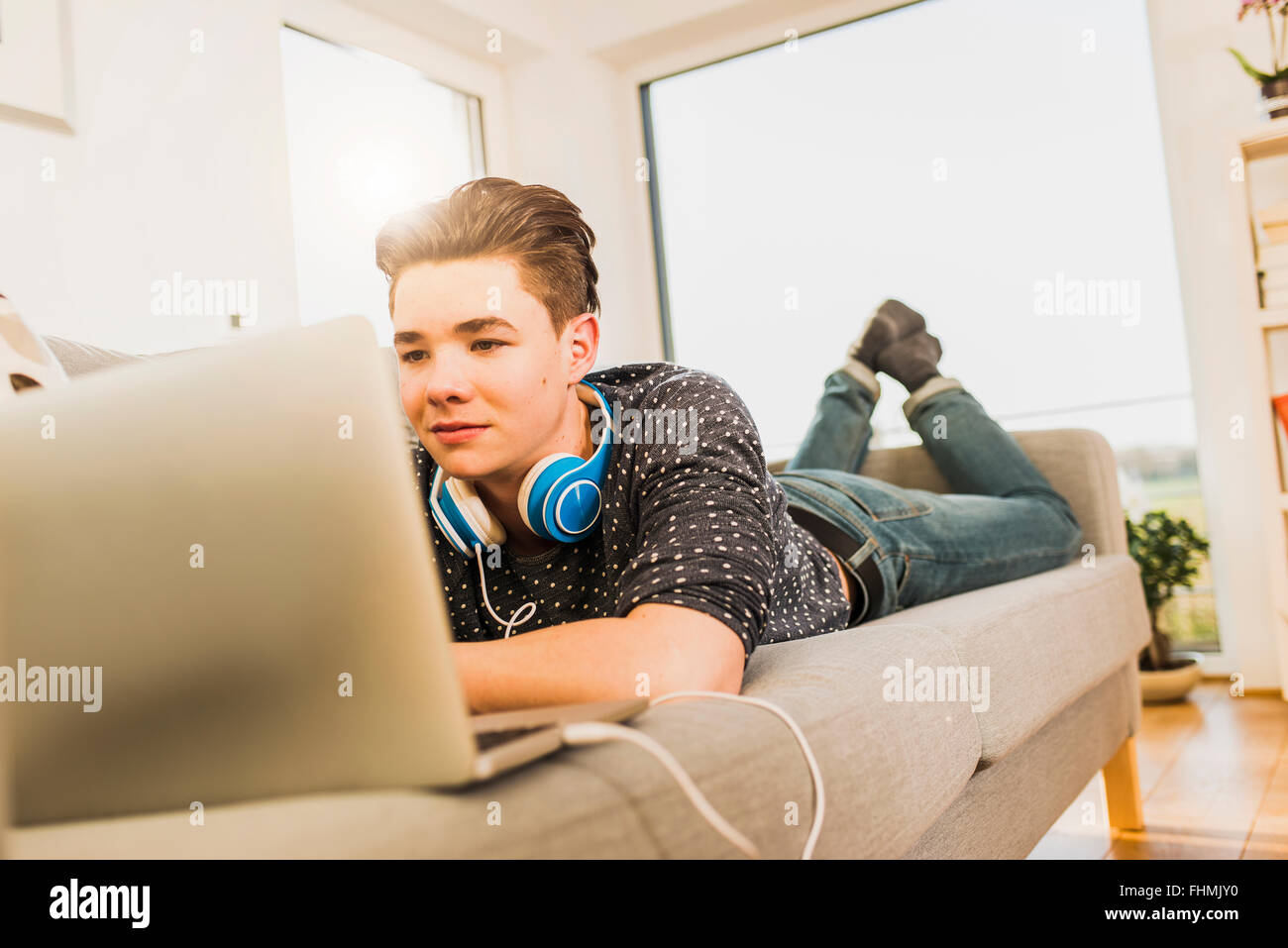 Young man lying on couch using laptop Stock Photo - Alamy