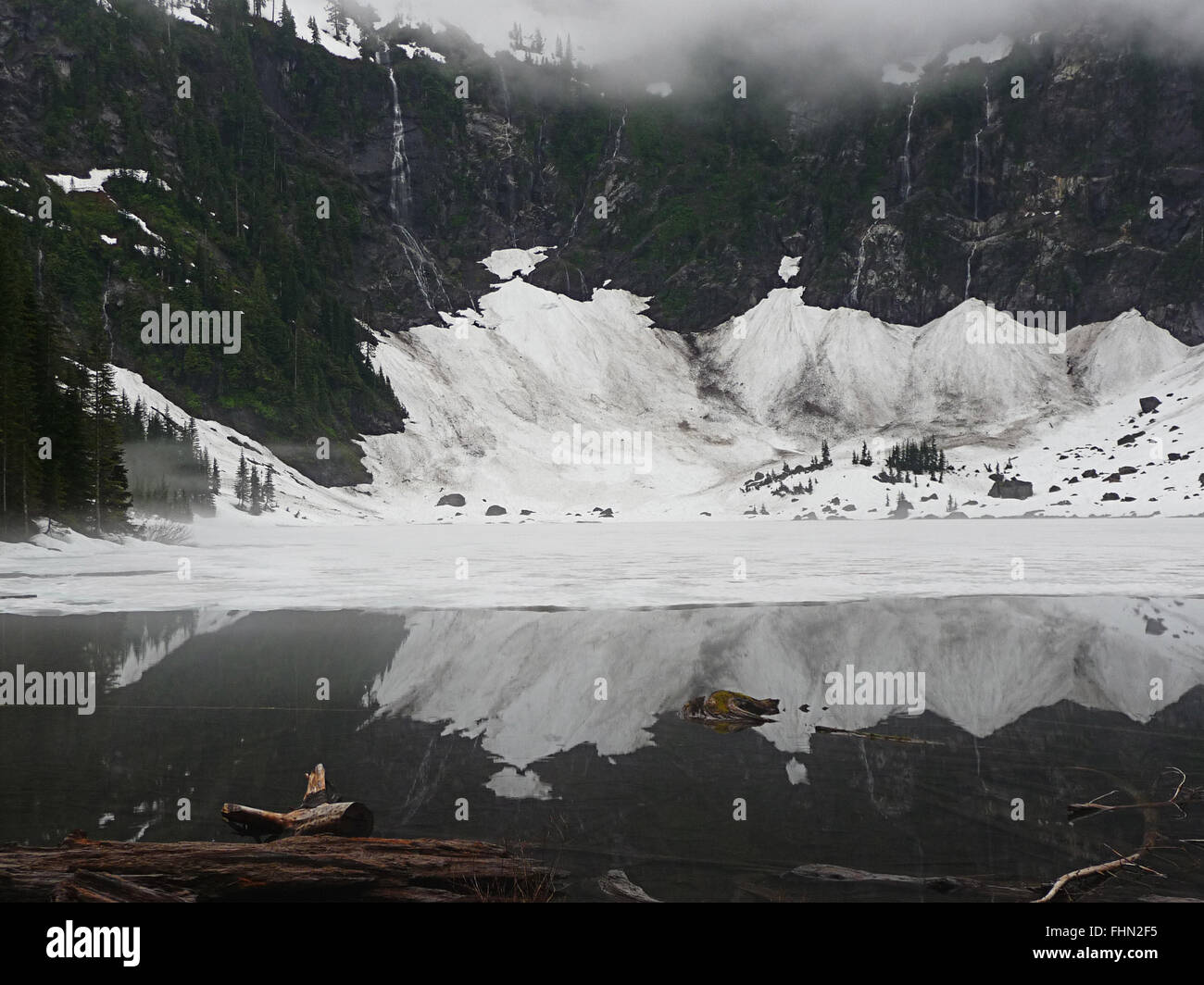 Snowy alpine lake with reflection, log in foreground Stock Photo - Alamy