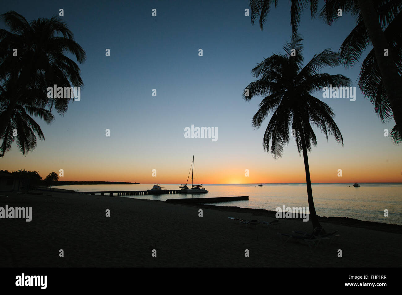 A bright orange sunset on a Cuban beach with the silhouettes of sailing ...
