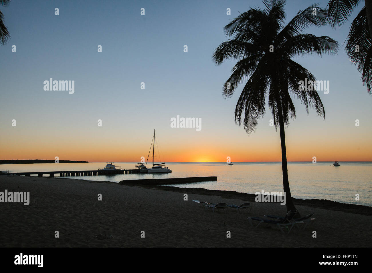 A bright orange sunset on a Cuban beach with the silhouettes of sailing ...