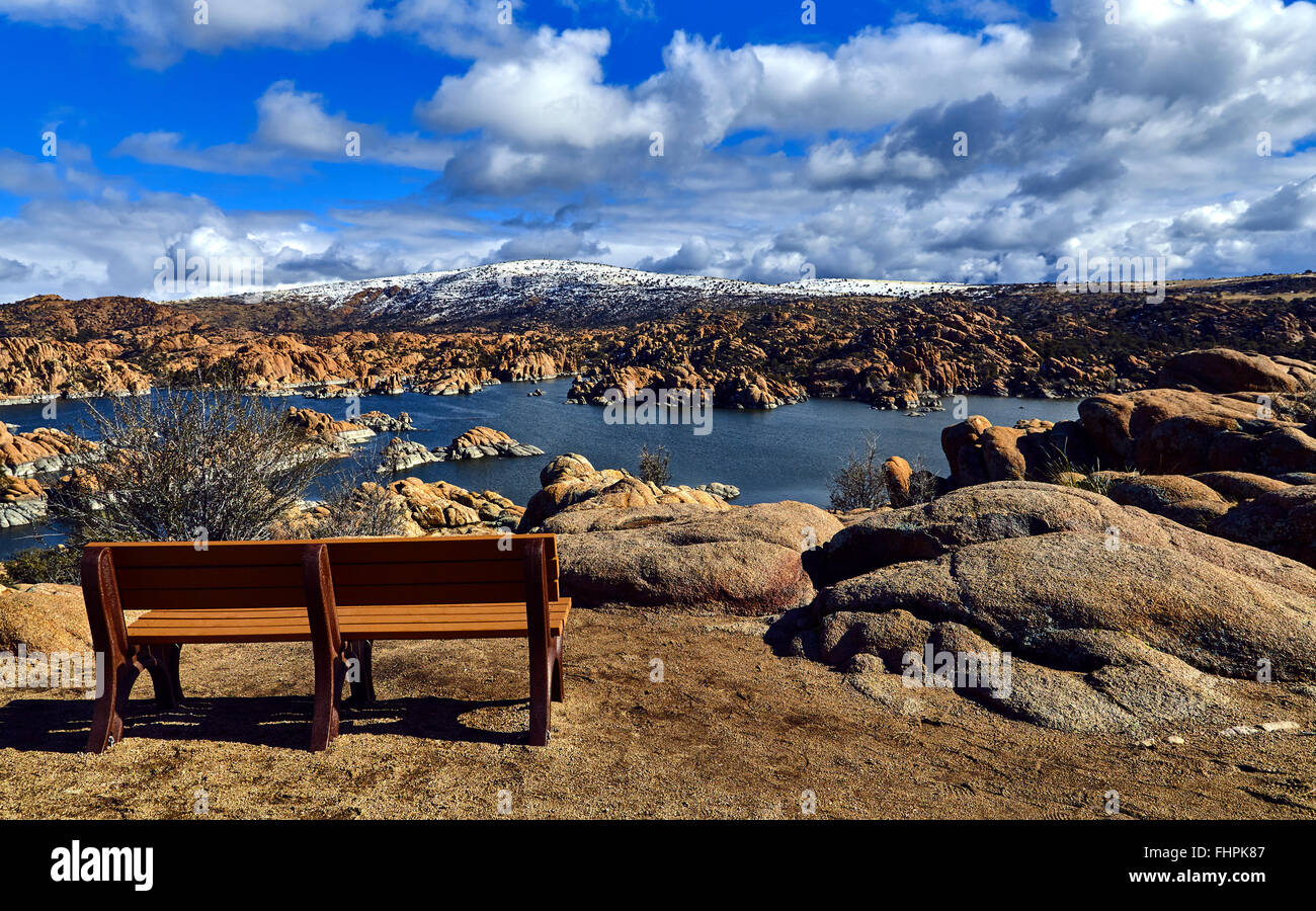 A bench overlooking a lake surrounded by boulders and a snowcapped ...