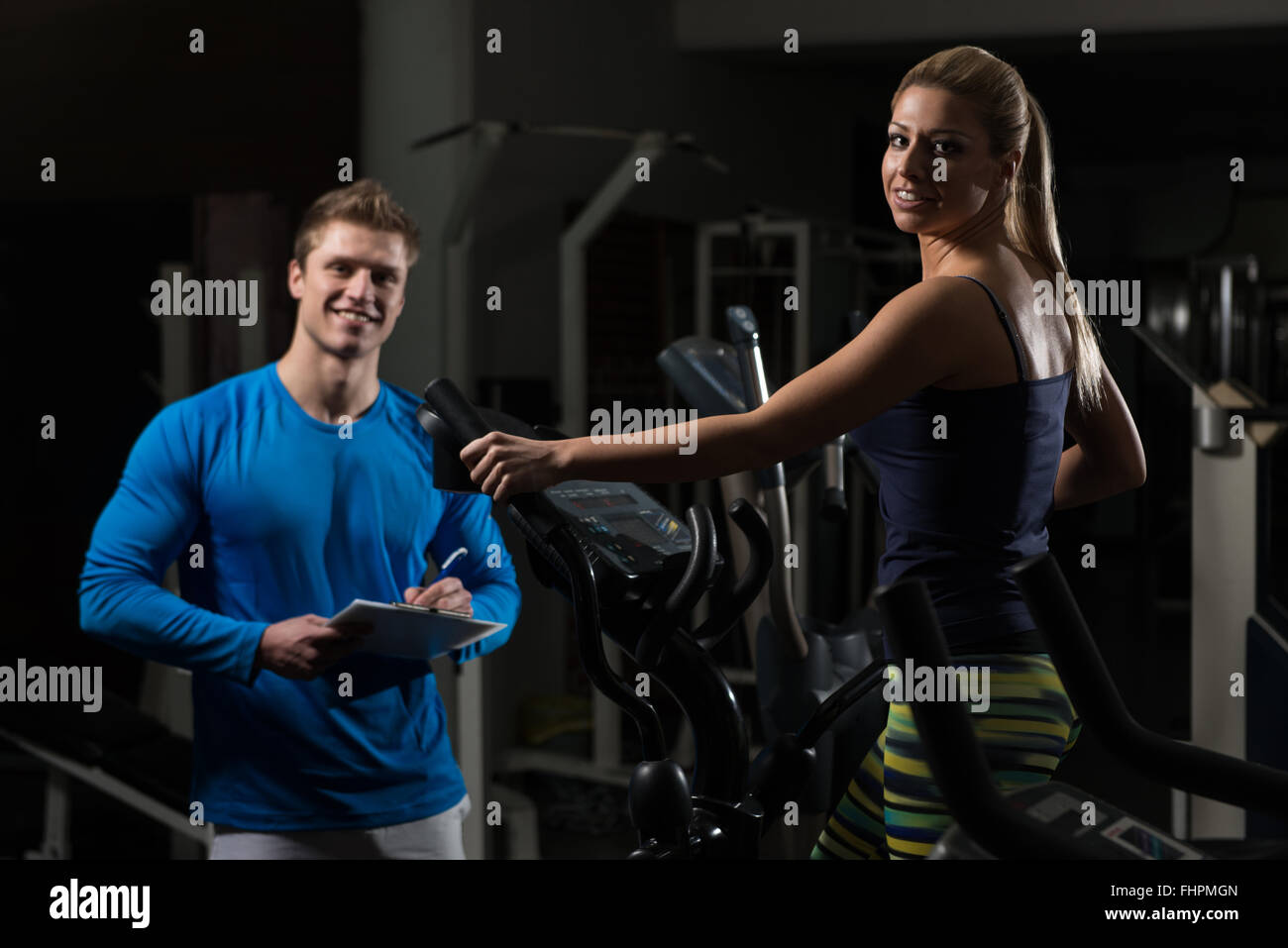 Young Woman Doing Aerobics Elliptical Walker In Gym And Personal ...