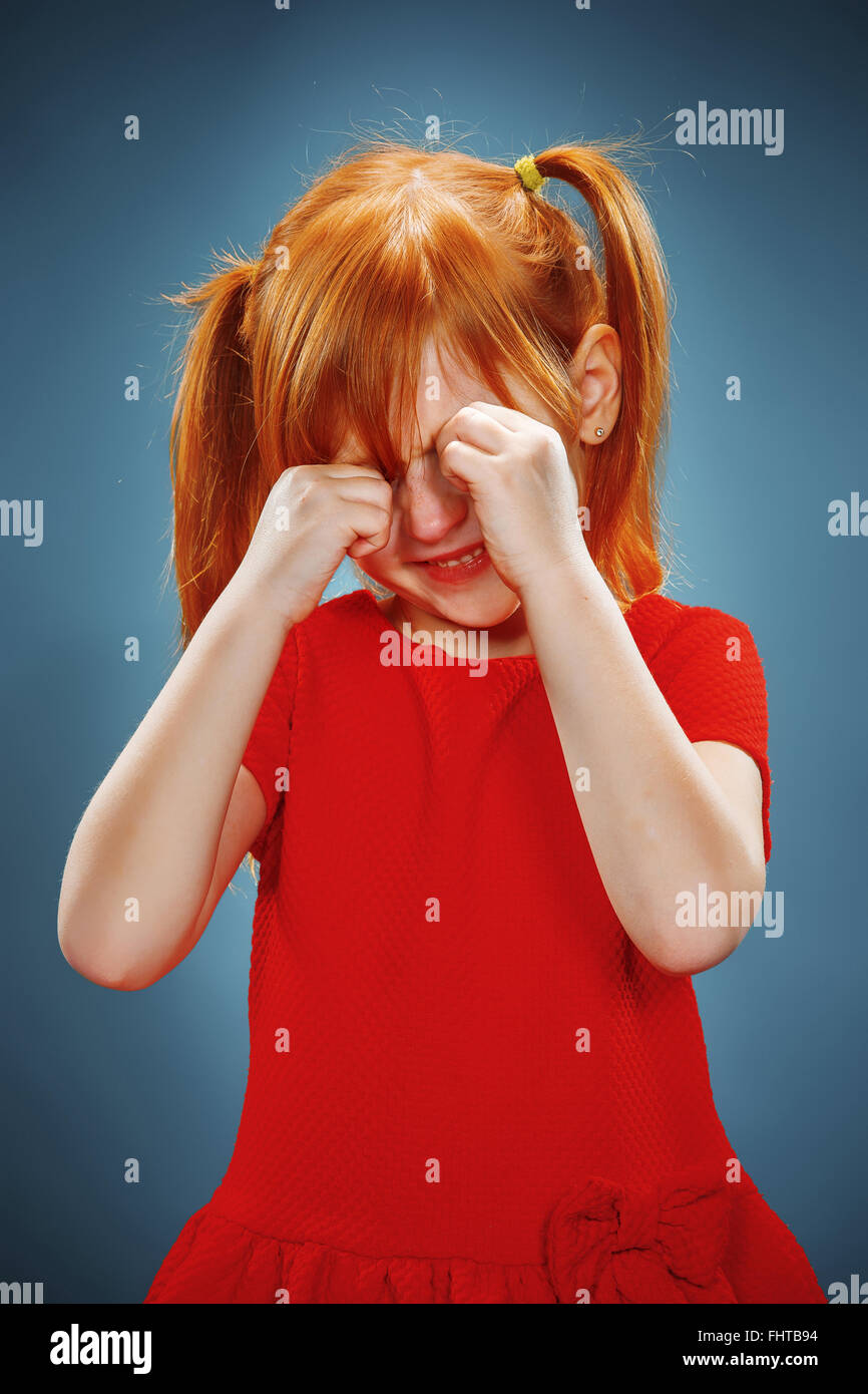 The portrait of a little girl in red dress on blue background. She is ...