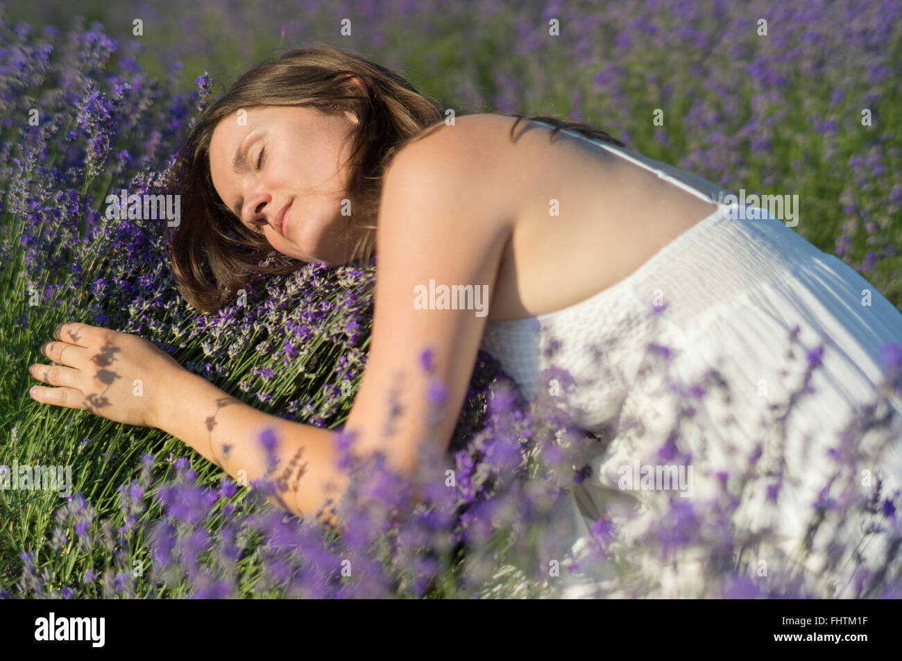 Beautiful young woman with a white dress hugging a lavender bush ...