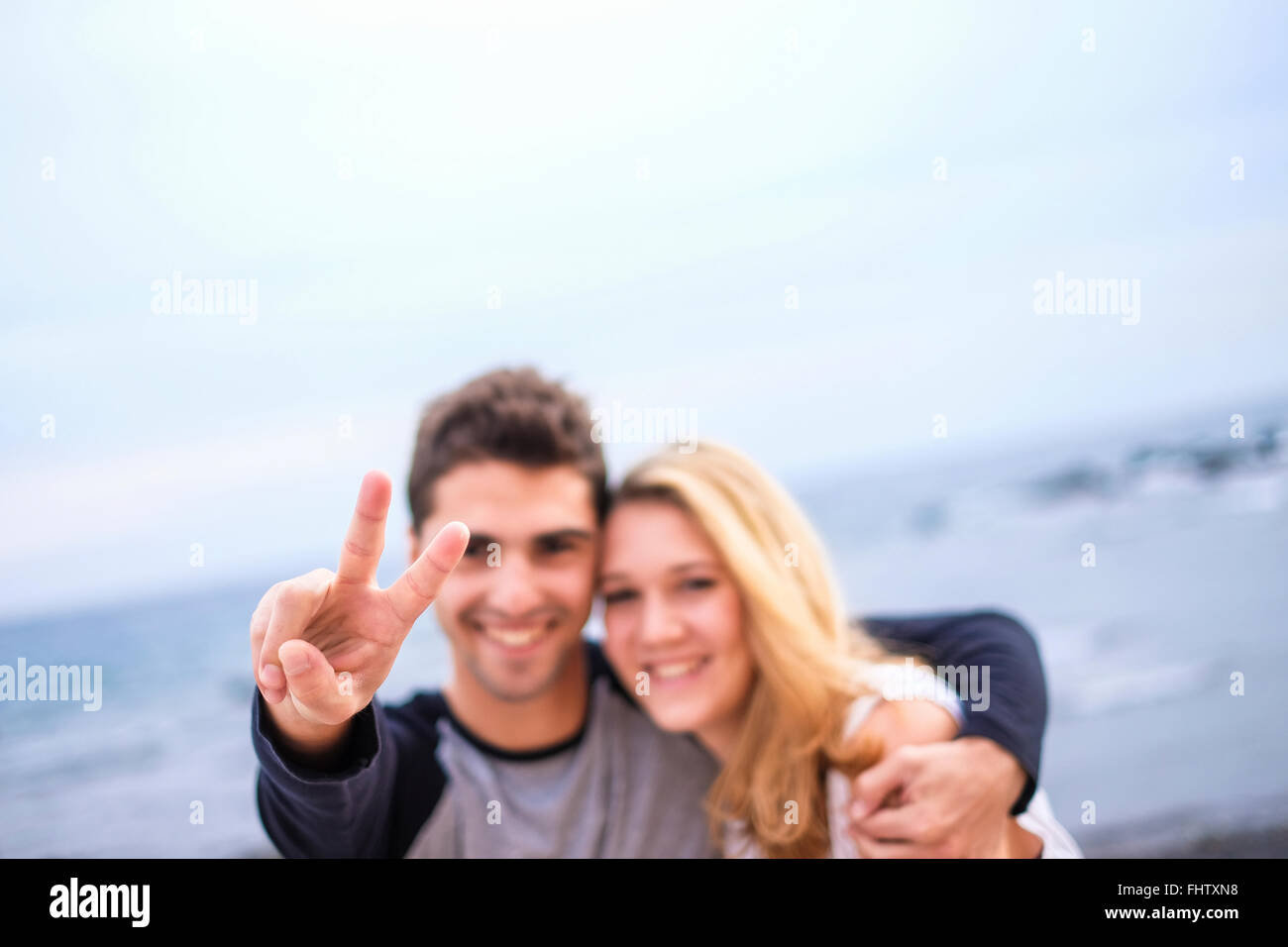 Happy young couple embracing and making victory sign Stock Photo - Alamy