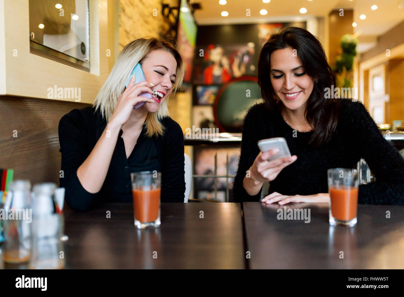 Two beautiful women talking on phone in cafe while being happy Stock ...