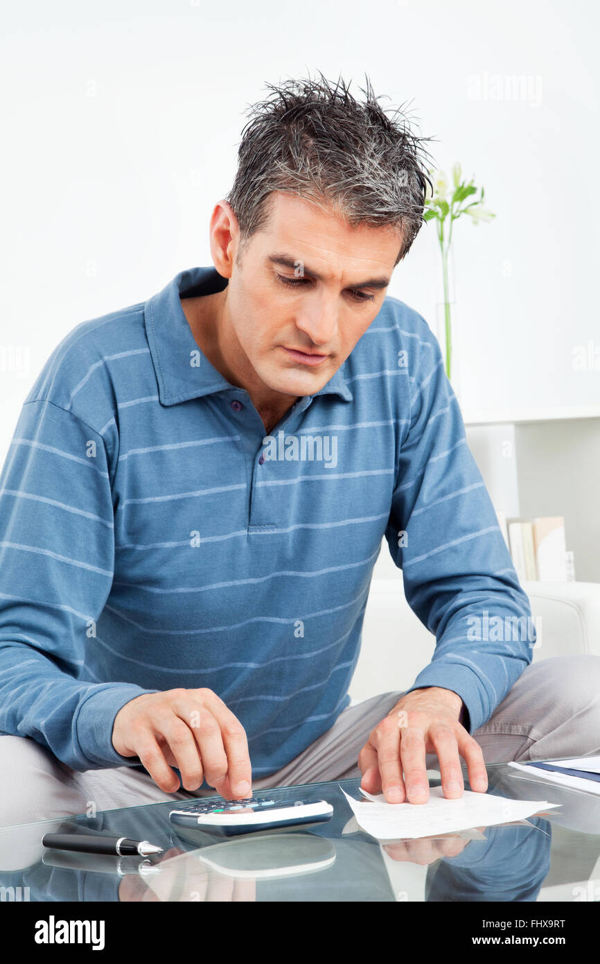 Man with calculator and bills on living room table Stock Photo - Alamy