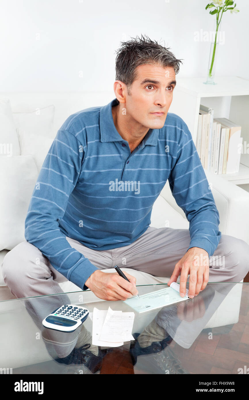 Senior man signing check on living room table Stock Photo - Alamy