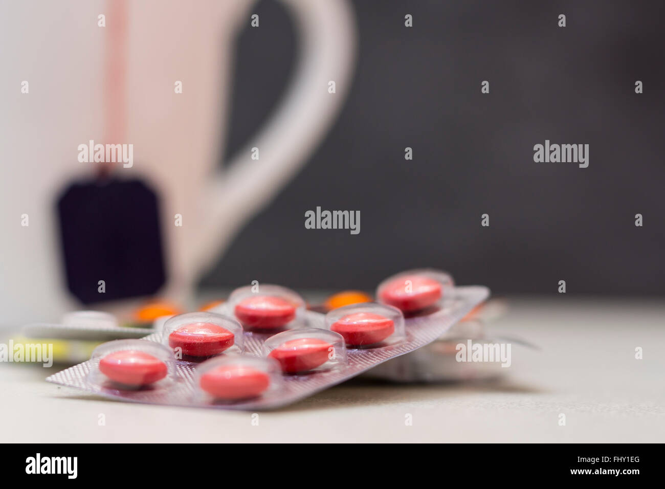 Red medication and a cup of tea in the background Stock Photo - Alamy
