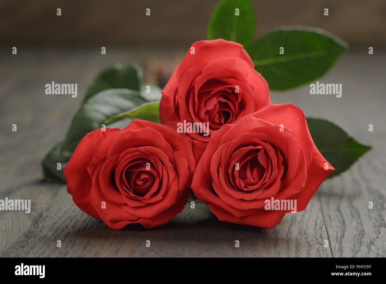 three red roses on wooden table Stock Photo - Alamy