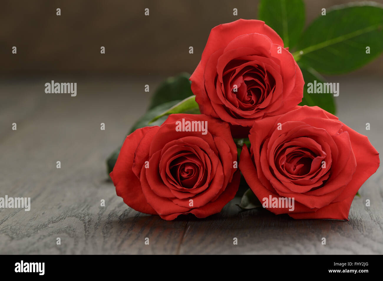 three red roses on wooden table Stock Photo - Alamy