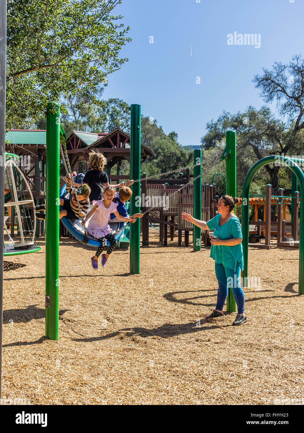 Four young kids having fun on a giant swing set that an adult female is ...