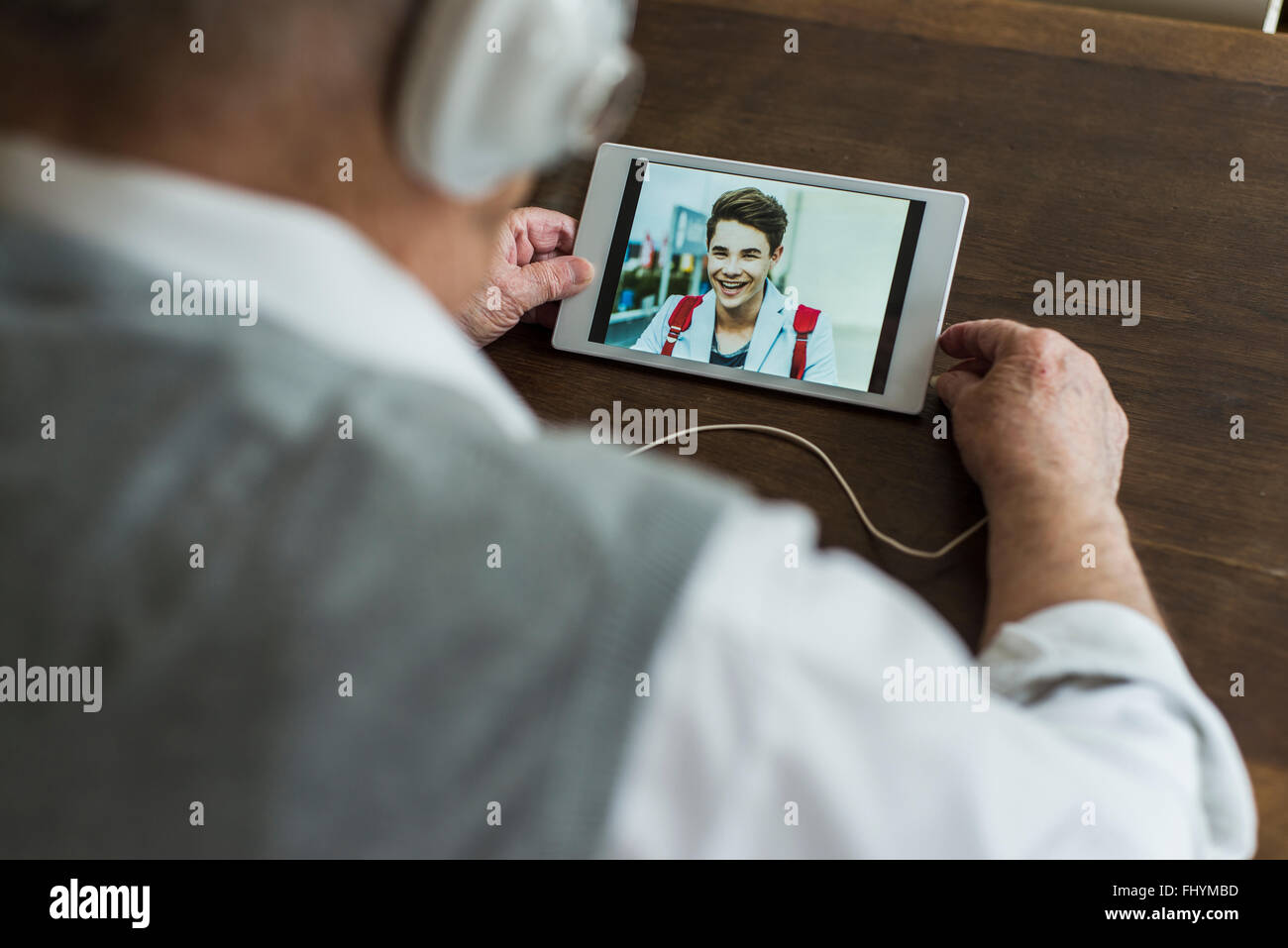 Senior man using mini tablet and headphones for skyping with his ...