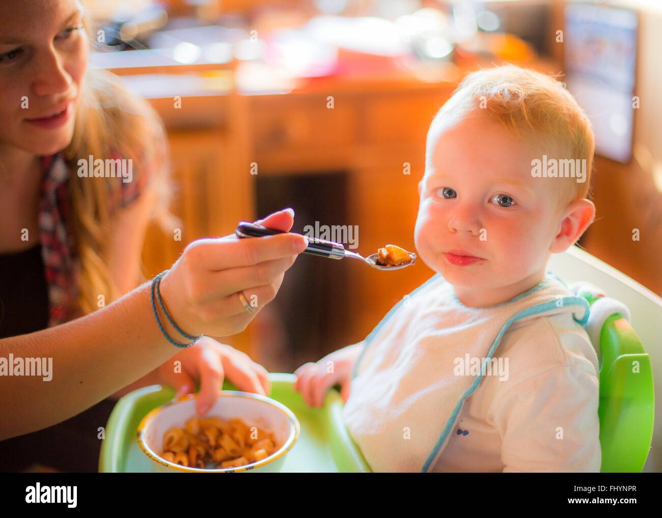 MODEL RELEASED. Mother feeding her toddler in a high chair Stock Photo ...