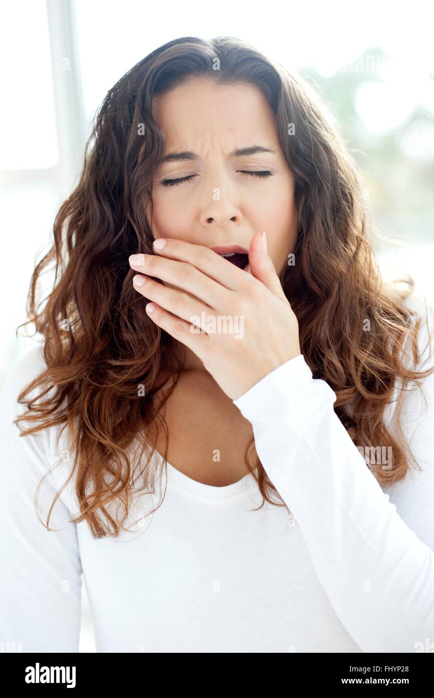 MODEL RELEASED. Mid adult woman yawning, covering mouth Stock Photo - Alamy