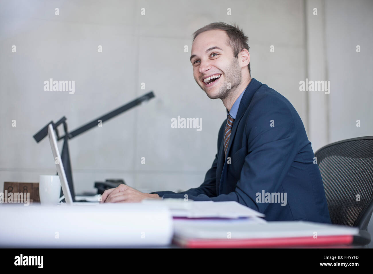 Laughing businessman at desk looking up Stock Photo - Alamy