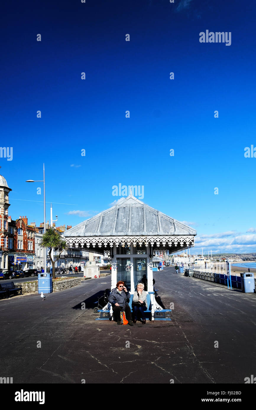 Two ladies catch up on in conversation in a pavilion on on the seafront ...