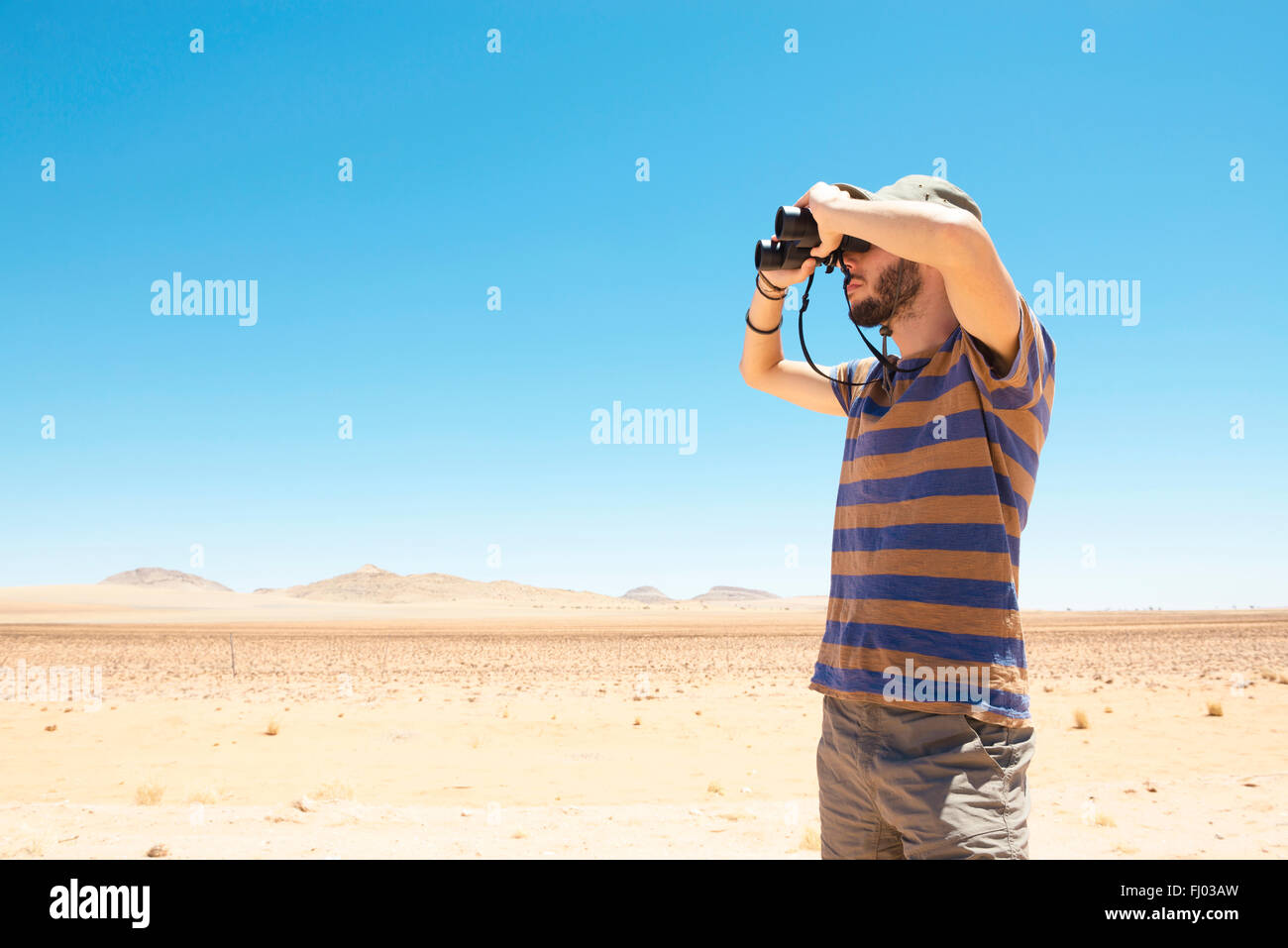 Namibia, Namib desert, man with hat using binoculars to look away Stock ...