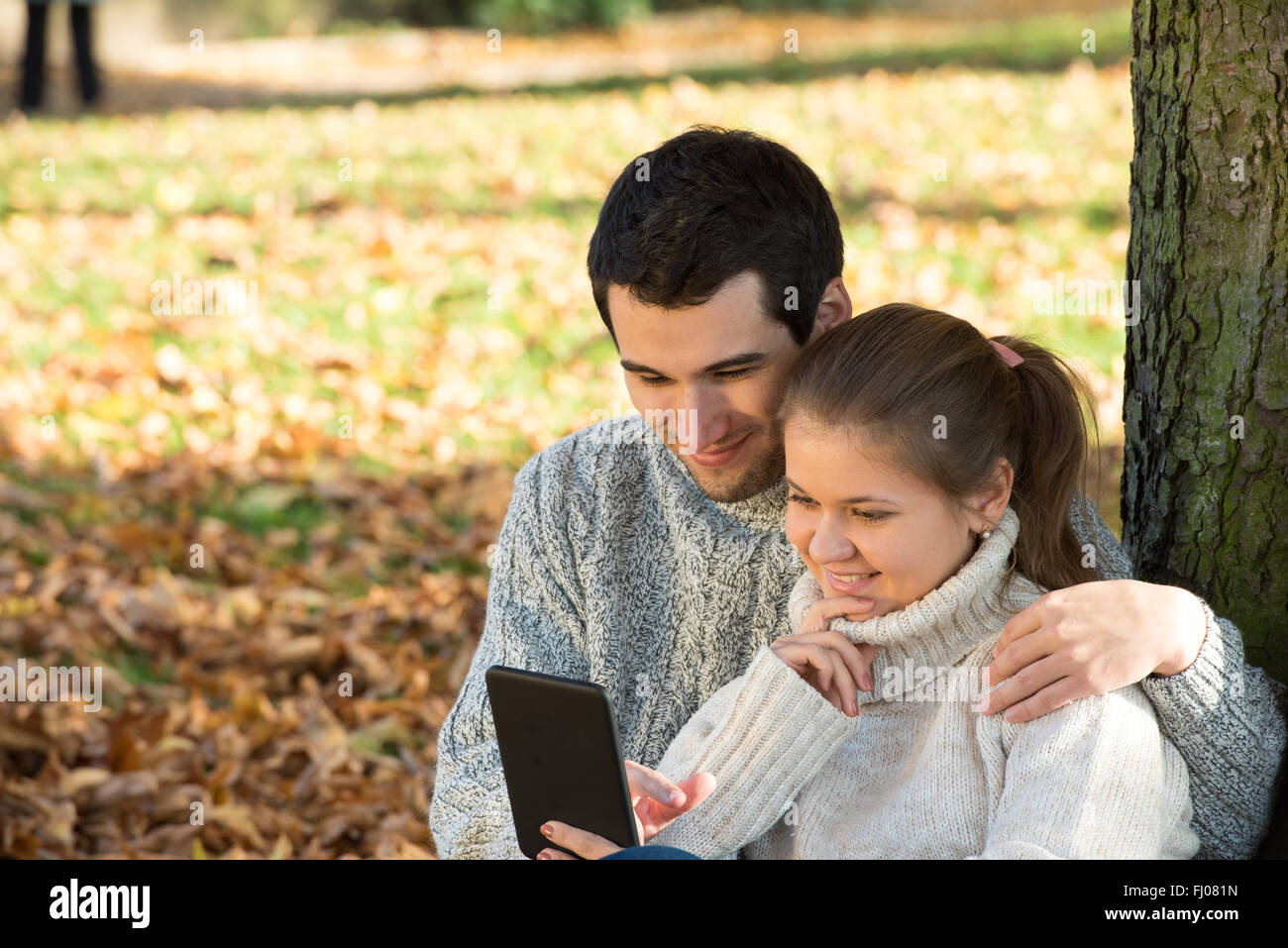 young couple in autumn park sitting near tree reading ebook Stock Photo ...