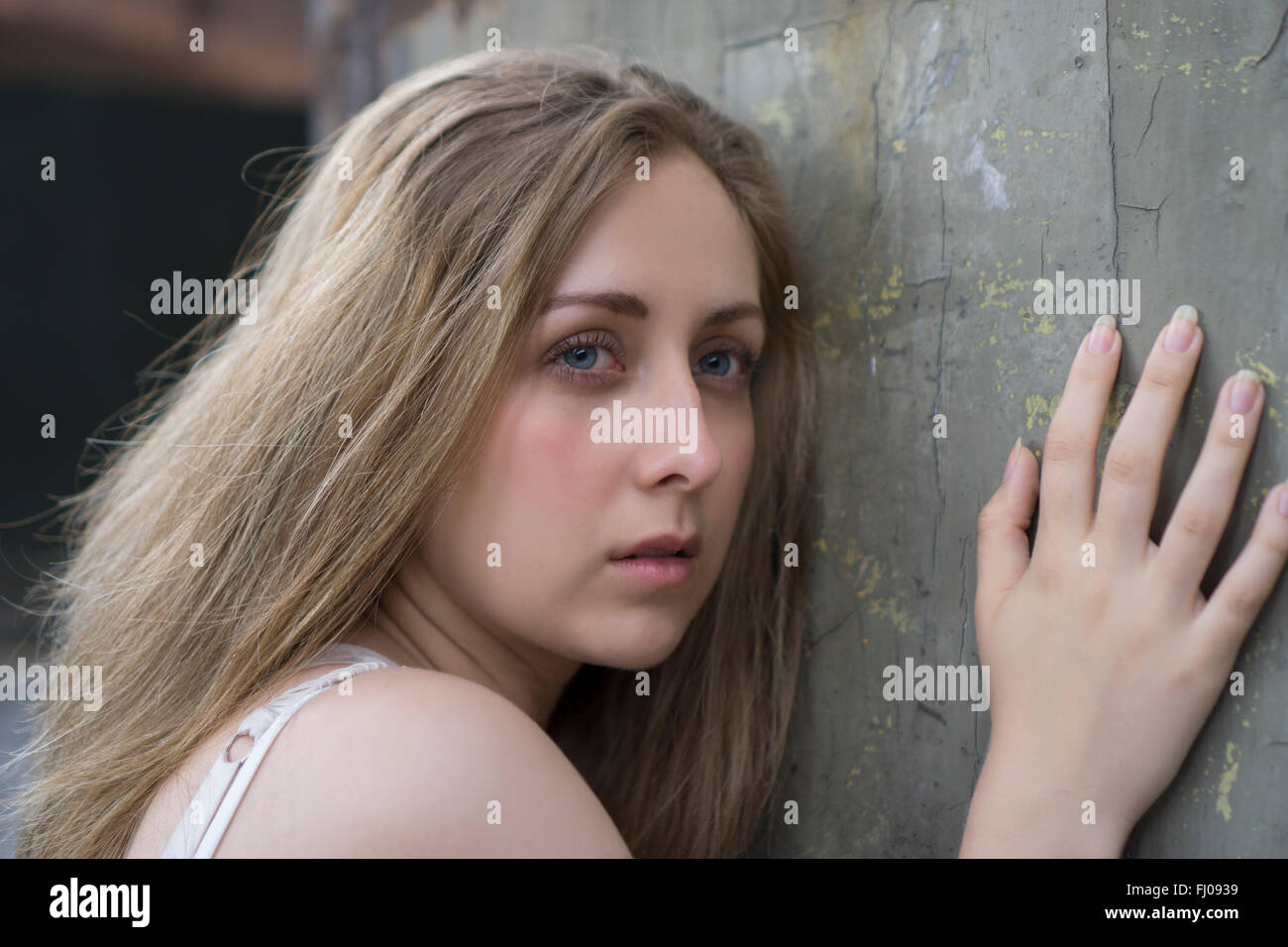 Scared young woman leaning against the wall Stock Photo - Alamy