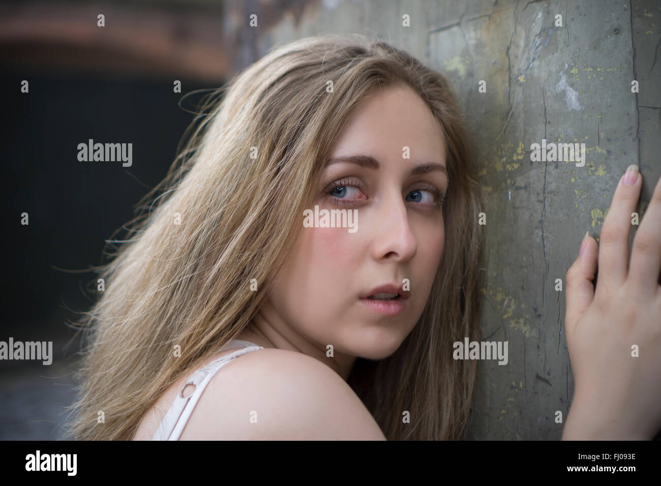 Scared young woman leaning against the wall Stock Photo - Alamy