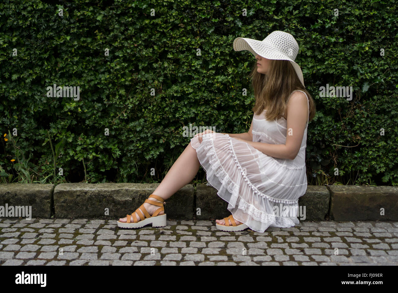 Woman in white dress and a hat sat by the hedge Stock Photo - Alamy