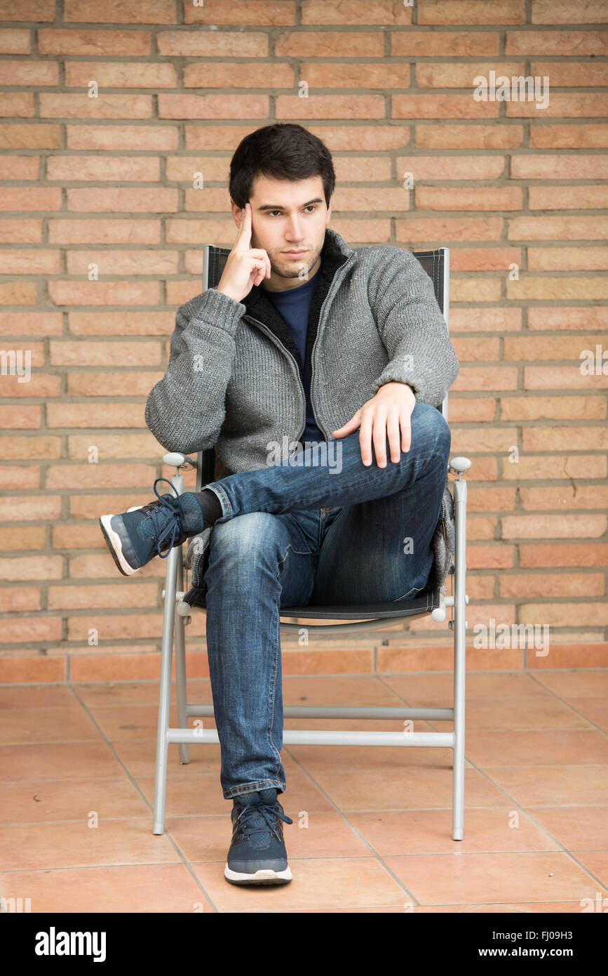 young man sitting in chair in front of bricks wall Stock Photo - Alamy