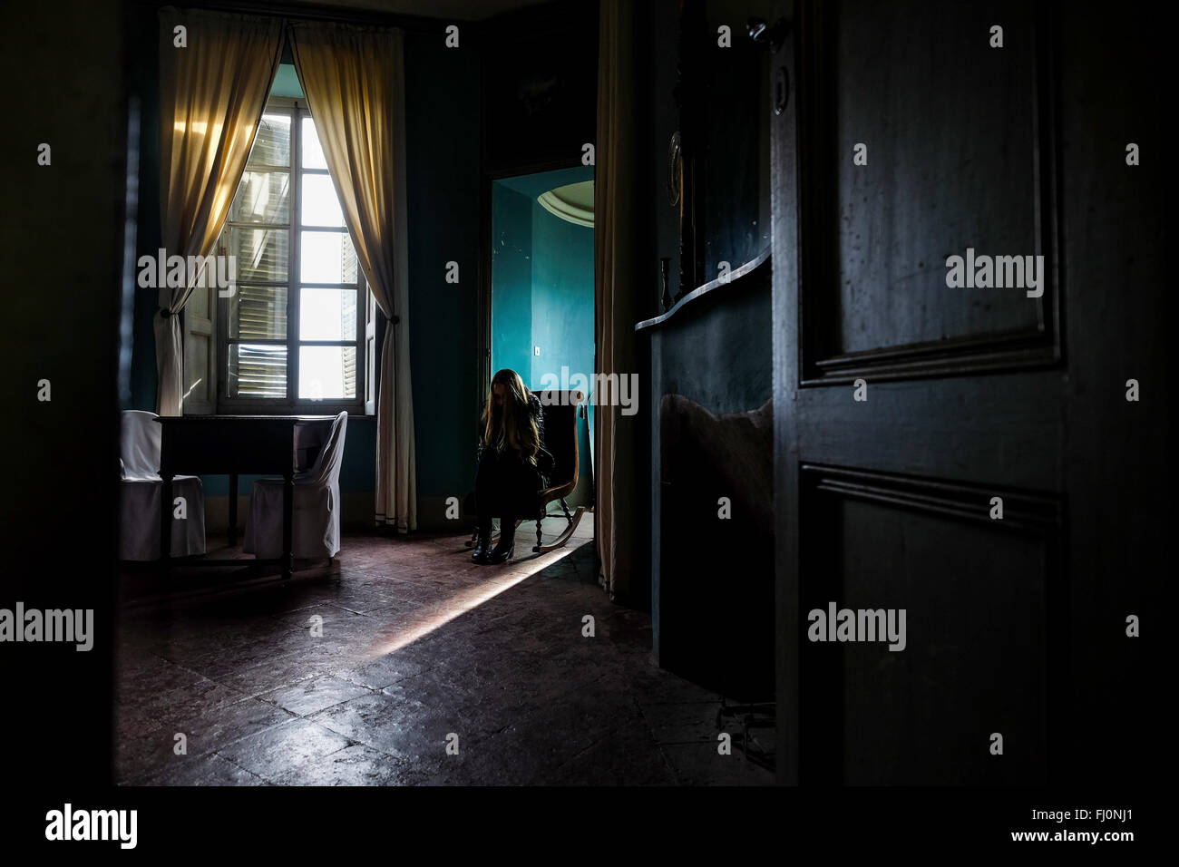 Young woman sitting in a gloomy room Stock Photo - Alamy