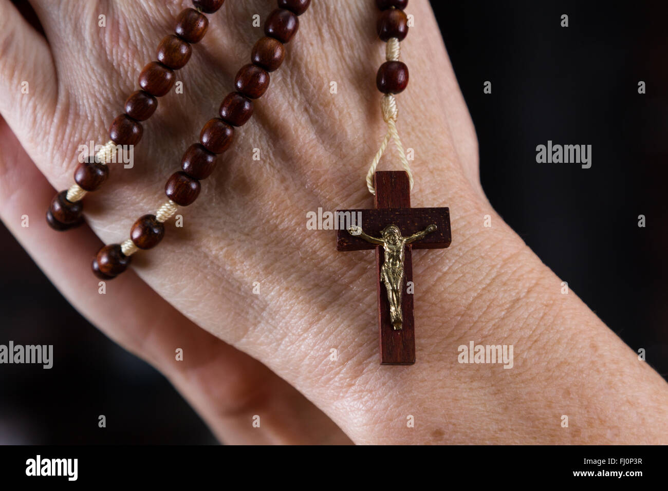 close up of a woman's hands holding rosary beads focused on the cross ...