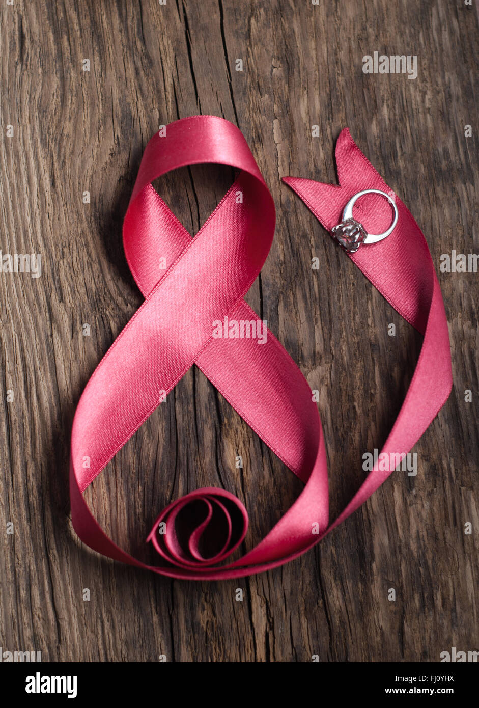 Beautiful pink ribbon with a ring on a wood background, greetings on ...
