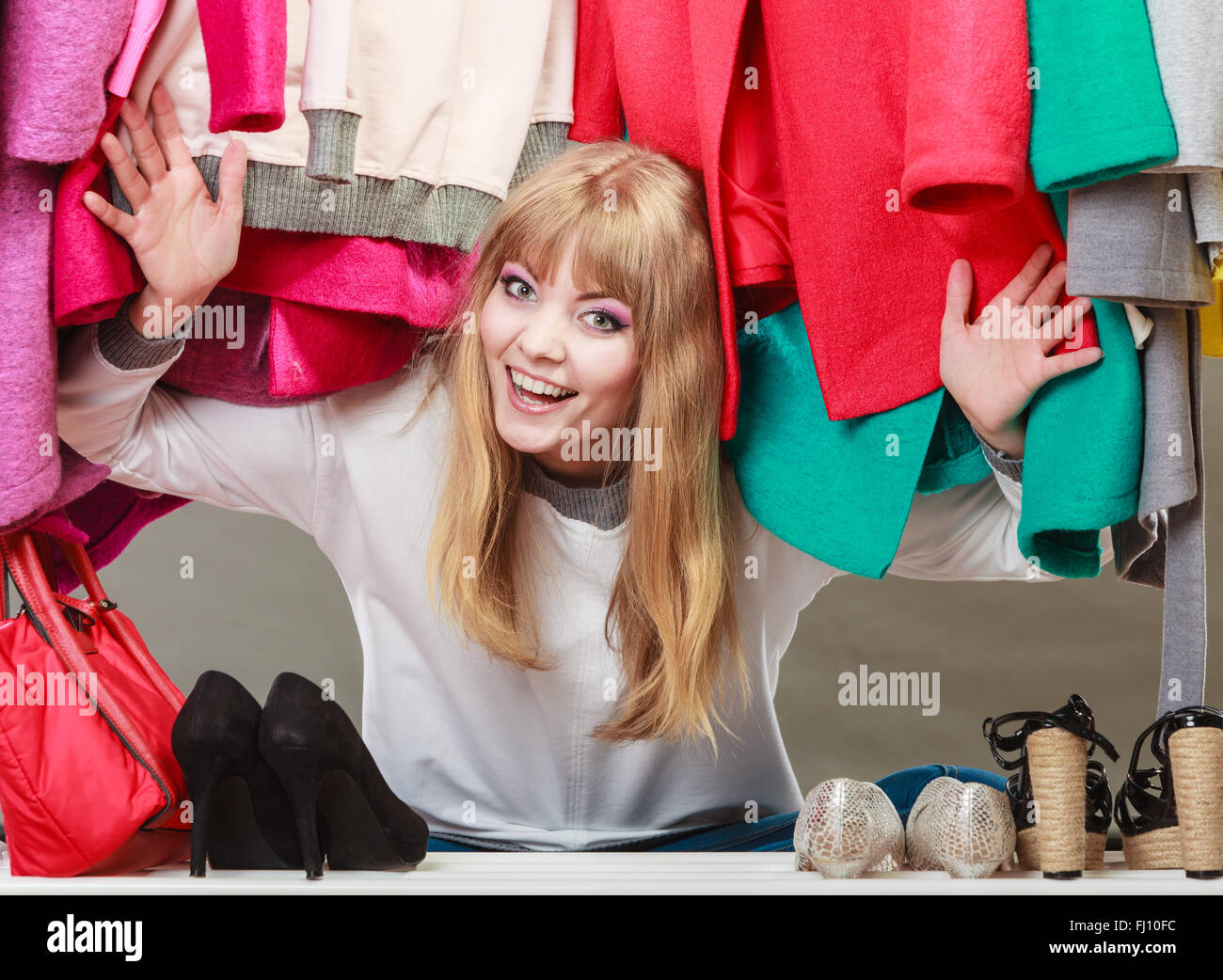Pretty woman sitting on the floor under clothing from wardrobe. Young ...