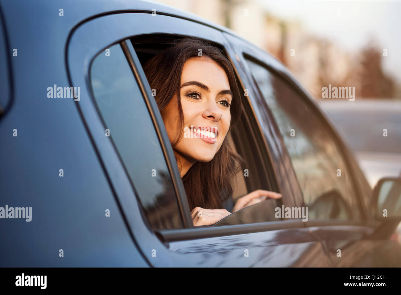 Smiling young woman looking out of car window Stock Photo - Alamy