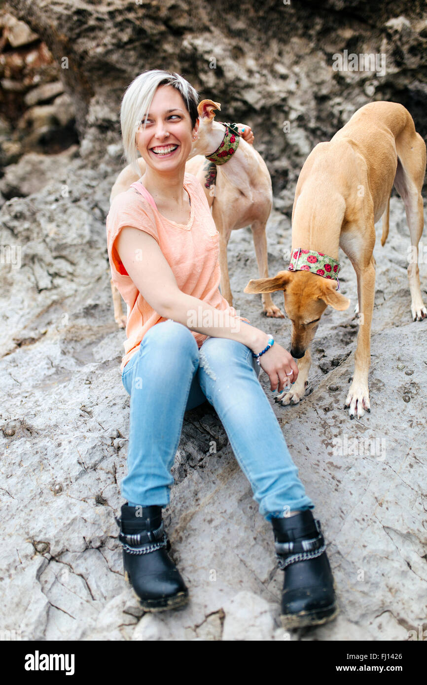 Spain, Llanes, portrait of laughing young woman with her greyhounds on ...