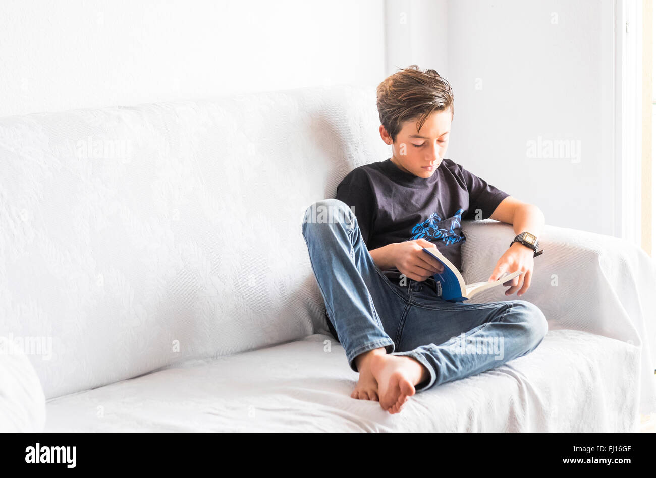 Boy sitting on a white couch reading a book Stock Photo - Alamy