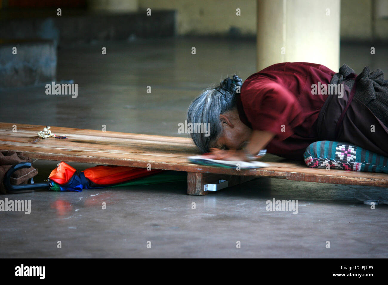 Old woman Buddhist Tibetan refugee praying on the floor in Mac leod ...